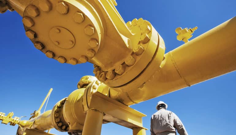 Male worker standing below yellow painted pipeline at oil refinery ...